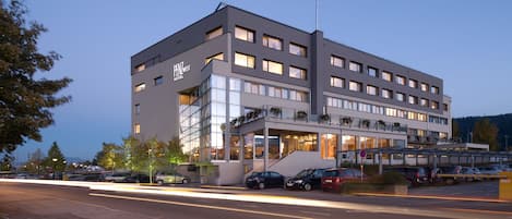 Um hotel moderno com entrada imponente, vários andares e área de estacionamento.
