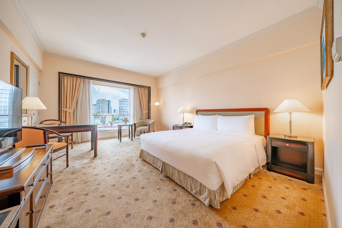 Quarto de hotel com uma cama grande, uma escrivaninha, uma cadeira, uma televisão e uma janela com vista para a cidade.