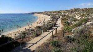 Uma praia costeira com um caminho de areia que leva à água, cercada por vegetação.