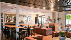 Uma área de bar moderna com mesas e banquetas de madeira, uma lareira e um espaço de estar com sofás de couro.