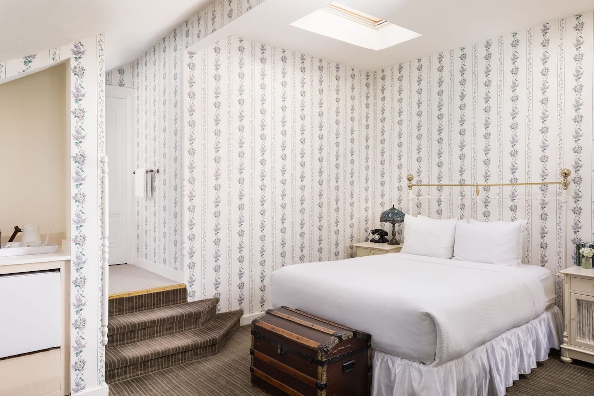 Quarto com uma cama grande, mala, mesa de cabeceira e banheiro com espelho e porta-toalhas.