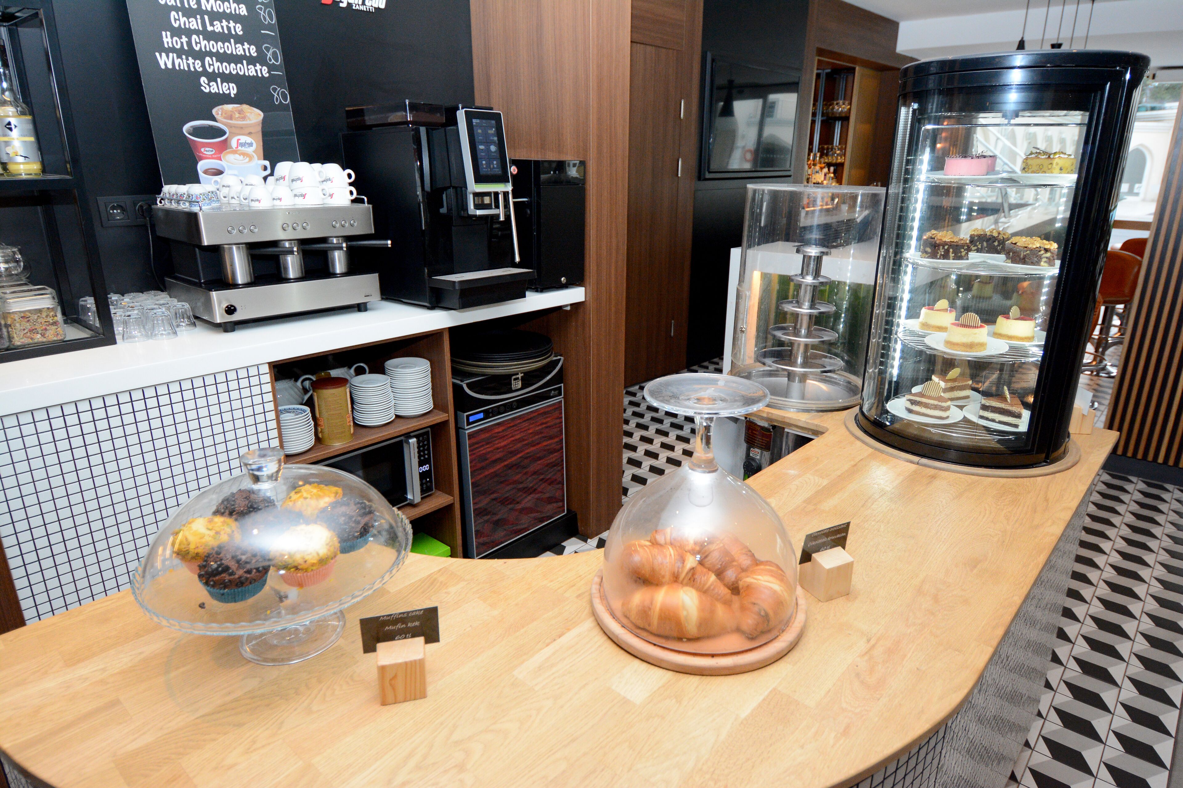 Um balcão de pastelaria com doces, uma máquina de café e uma vitrine com sobremesas.