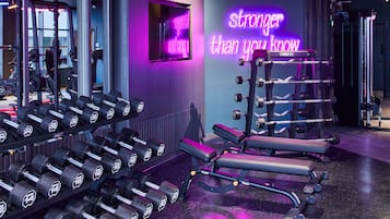 Uma academia com equipamentos de musculação, um letreiro de neon e um espelho.