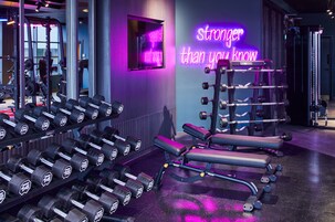 Uma academia com equipamentos de musculação, um letreiro de neon e um espelho.