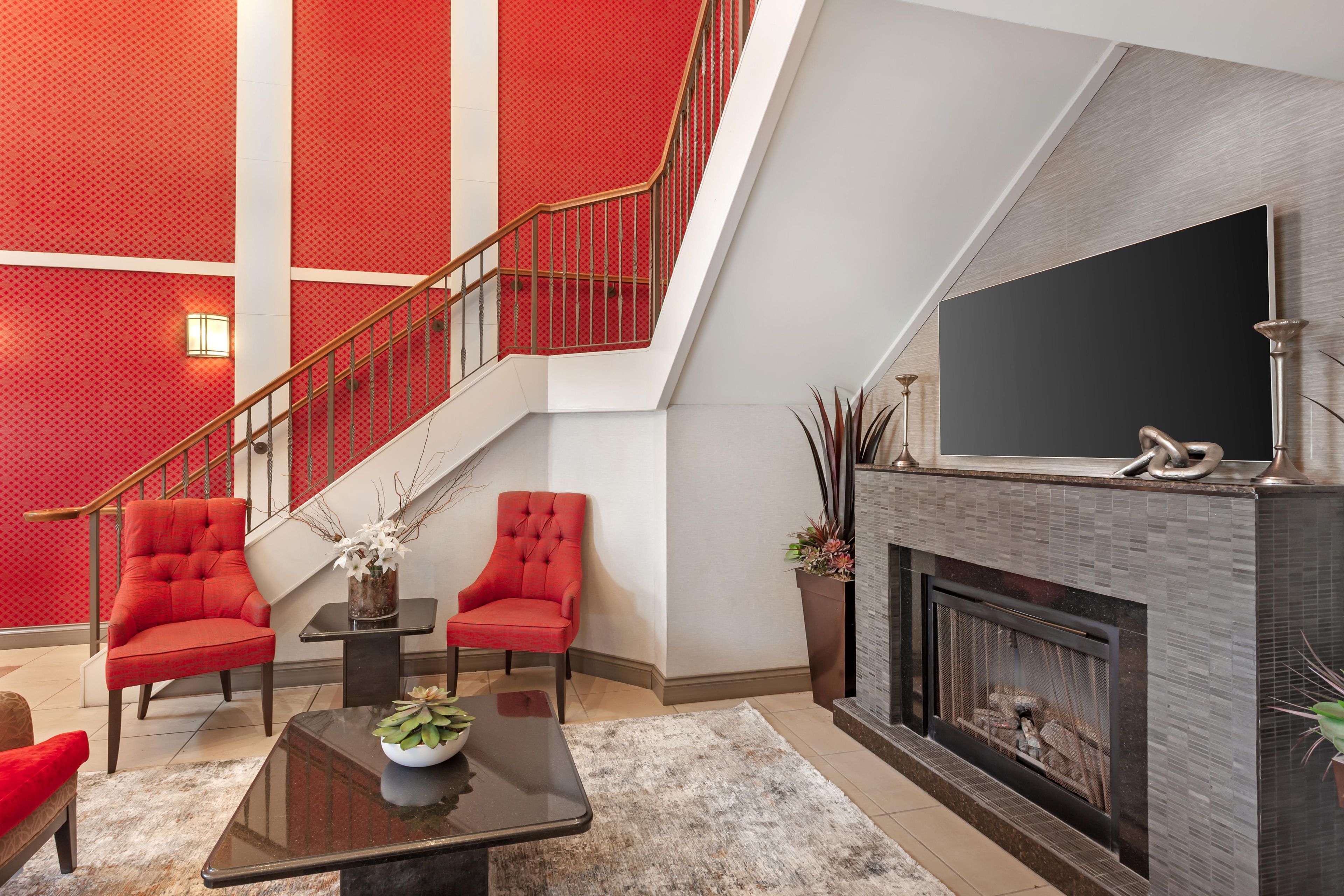 Uma sala de estar moderna com lareira, poltronas estofadas em vermelho, televisão de tela plana e escada com paredes em padrão vermelho.