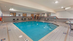 Piscina interior com faixas delimitadoras claras, avisos de segurança e cadeira do salva-vidas.