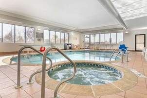 Piscina interna com hidromassagem, sinalização clara e vista para o exterior através de grandes janelas.