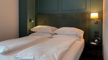 Uma cama bem arrumada com lençóis e almofadas brancos, um abajur e um telefone em uma mesinha ao lado da cama.