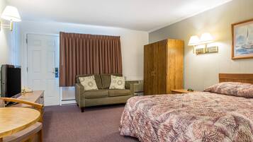 Quarto de hotel com cama, sofá, guarda-roupa de madeira, escrivaninha com cadeira e televisão.