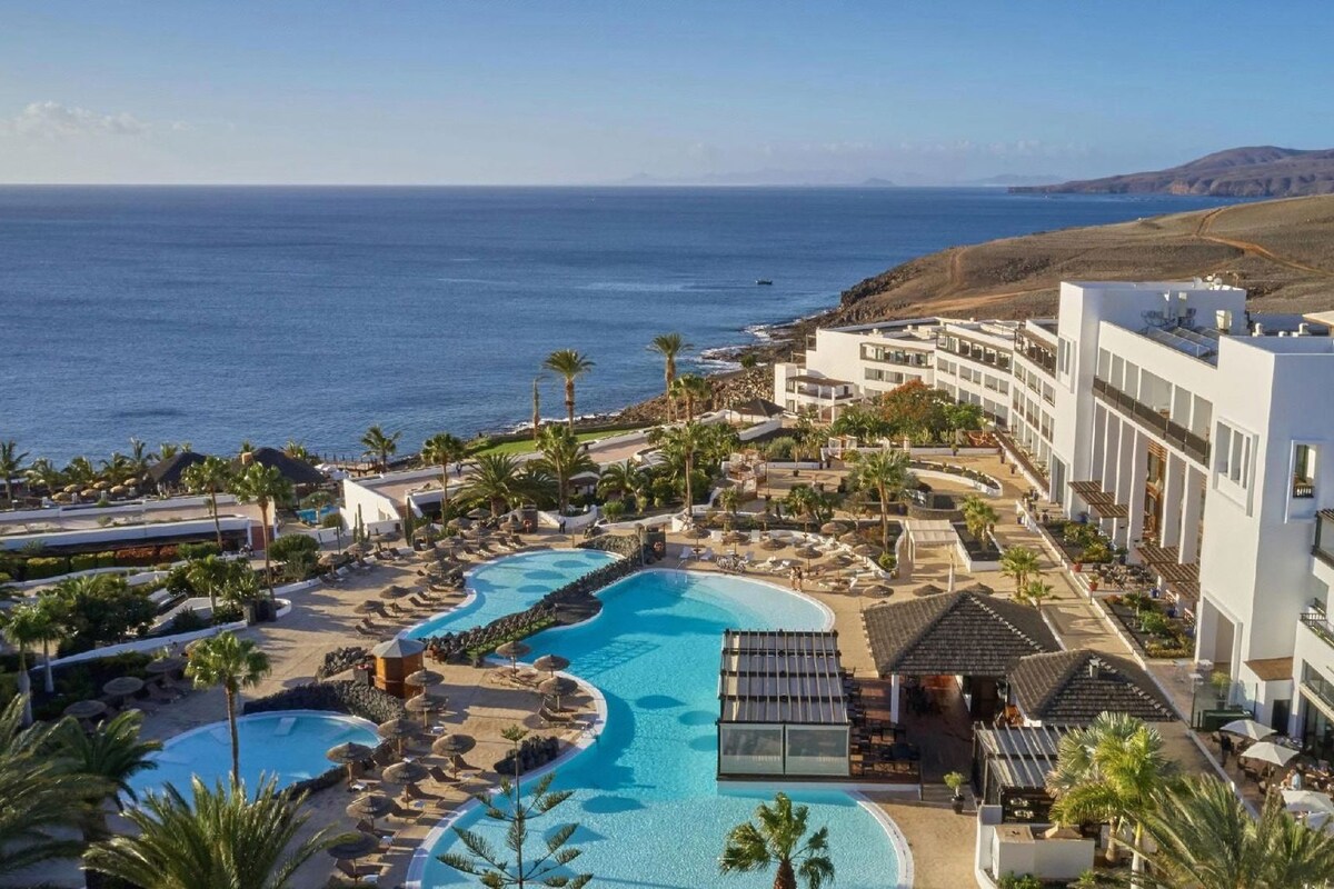 Um resort com várias piscinas, uma área de praia e vista para o oceano.