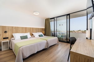 Quarto de hotel moderno com duas camas, uma escrivaninha e uma grande porta de vidro deslizante para a varanda.