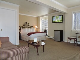 Quarto de hotel com cama, televisão, frigorífico, mesa de centro e uma cadeira.