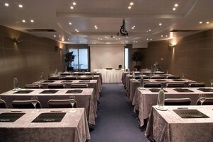 Uma sala de conferências com mesas, cadeiras dispostas em fileiras e um pódio na frente.