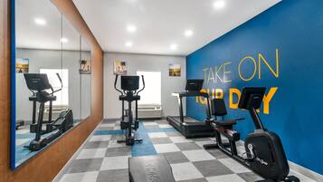 Academia com equipamentos de exercícios, parede azul com texto motivacional e piso xadrez.