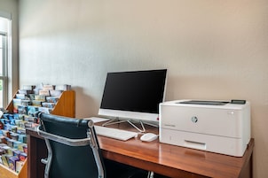 Uma mesa com um computador, uma impressora e uma cadeira.