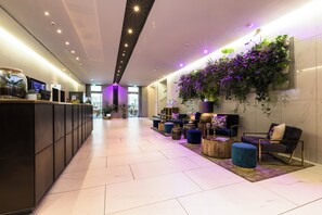 Um lobby moderno com uma receção, área de estar e um painel de plantas na parede.