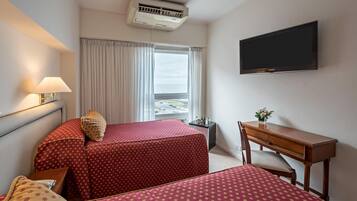 Quarto de hotel com duas camas, uma mesa, uma televisão e uma janela com cortinas.