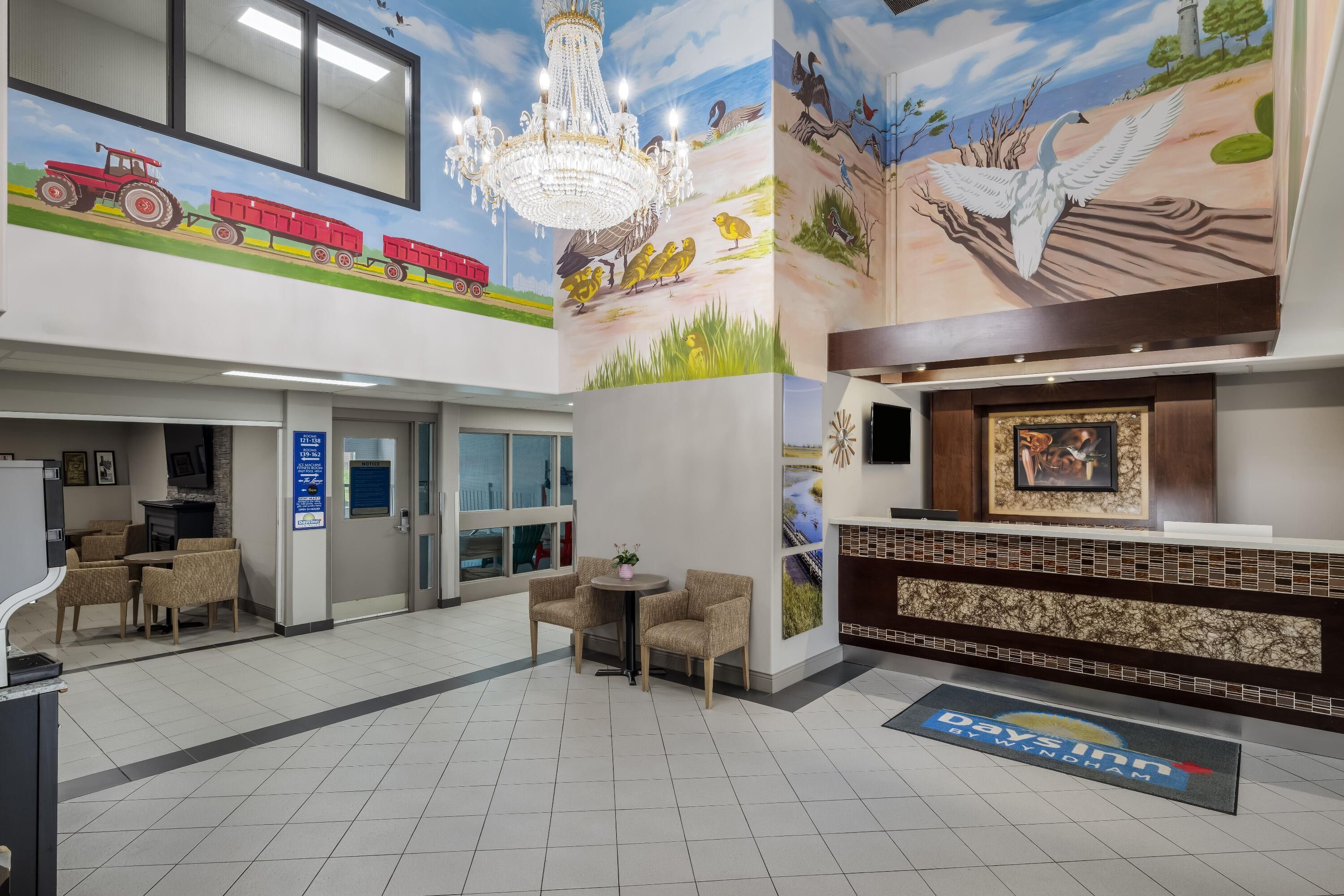 Um saguão de hotel com um candelabro, uma mesa de recepção e um mural de pássaros.