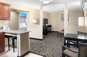 Quarto de hotel com cozinha compacta, cama, televisão, escrivaninha e área de refeições.