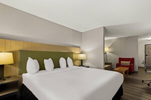 Quarto de hotel com uma cama grande, abajures, uma escrivaninha, uma cadeira e uma poltrona vermelha.