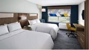 Quarto de hotel com duas camas, uma mesa, uma cadeira e uma janela com vista.