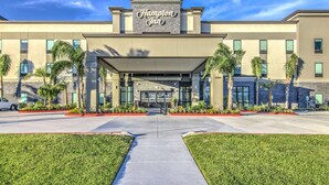 Um hotel Hampton Inn com fachada moderna, entrada central e estacionamento.