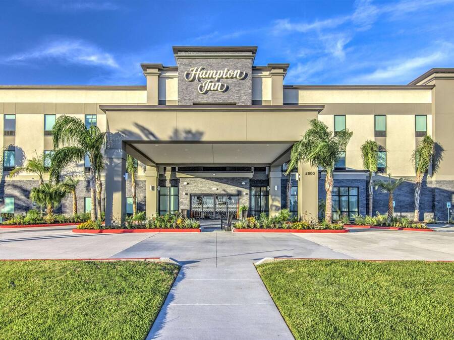 Um hotel Hampton Inn com fachada moderna, entrada central e estacionamento.