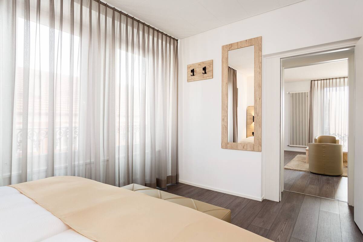 Quarto de hotel moderno com uma cama grande, um espelho e vista para o corredor.