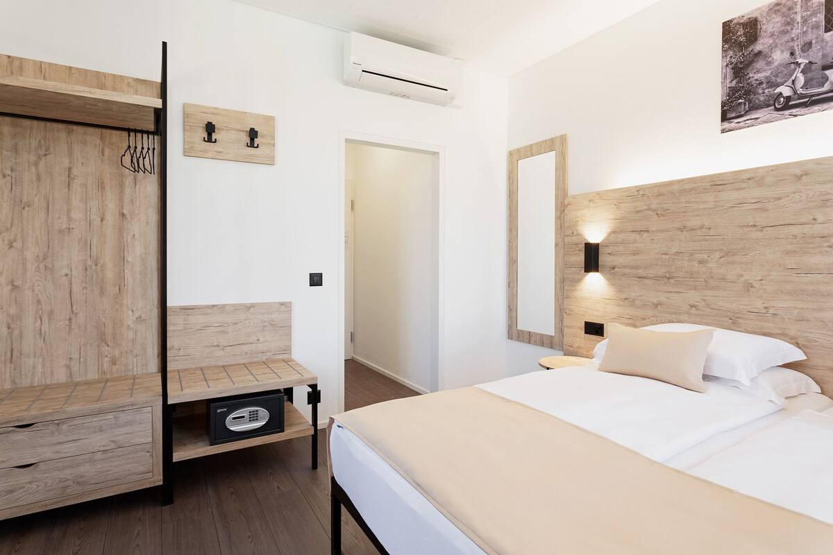 Quarto de hotel moderno com guarda-roupa de madeira, cama com roupa de cama branca e espelho fixado na parede.