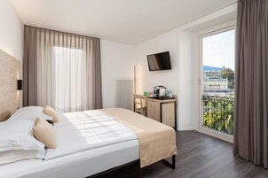 Quarto de hotel moderno com uma cama grande, uma escrivaninha, uma televisão e varanda com vista para a cidade.
