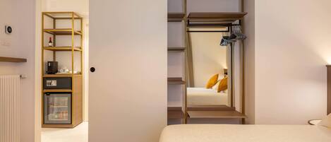 Quarto com cama, guarda-roupa, estante e um pequeno frigorífico.