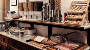 Uma mesa de buffet com diversos alimentos, incluindo uma seleção de pães, carnes e um canto para café.