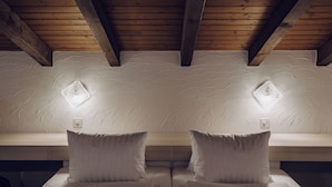 Quarto com teto de madeira, duas mesas de cabeceira e duas luminárias fixadas na parede.