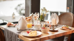 Uma mesa de pequeno-almoço posta com pratos, copos, uma vela e um vaso de flores.