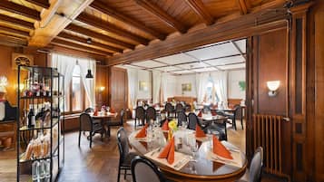Uma sala de jantar ampla, com vigas de madeira, várias mesas postas e uma variedade de cadeiras.