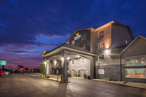 Hotel com design moderno, exibindo uma placa grande com a palavra 'Quality', uma entrada coberta e estacionamento.