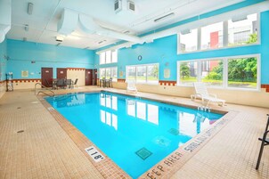Uma piscina interior com água azul cristalina, rodeada por chão e paredes revestidas em azulejos. Há espreguiçadeiras e uma mesa com cadeiras perto da piscina.
