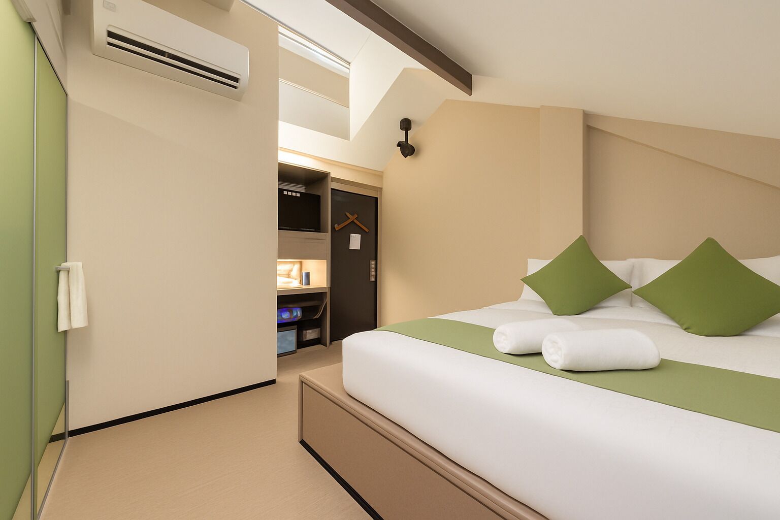 Quarto de hotel com cama, almofadas verdes, mesa de cabeceira, guarda-roupa e ar condicionado.