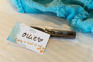 Embalagem de petiscos para cães com uma etiqueta que diz 'Olive' e 'Aproveite um agrado por nossa conta!'.