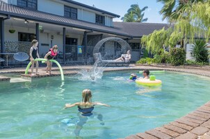 Uma área de piscina com um recurso aquático, espreguiçadeiras e um espaço de estar coberto.