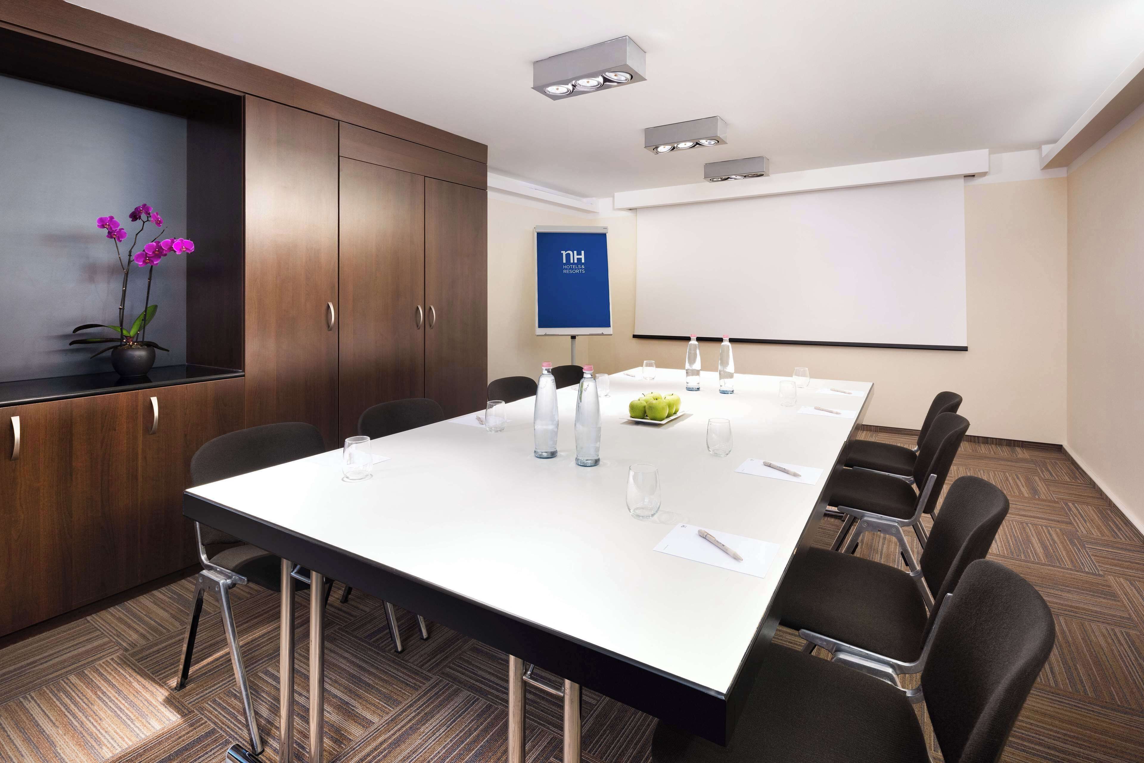 Uma sala de conferências com uma mesa comprida, cadeiras, uma tela de projetor e um letreiro com o nome do hotel.