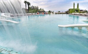 Uma grande piscina ao ar livre com cascata, cercada por espreguiçadeiras e palmeiras.