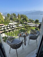 Uma varanda com duas cadeiras de vime, uma mesa pequena e vista para um lago e montanhas.