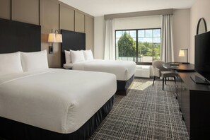 Quarto de hotel com duas camas, uma escrivaninha, uma cadeira e uma janela grande com vista.