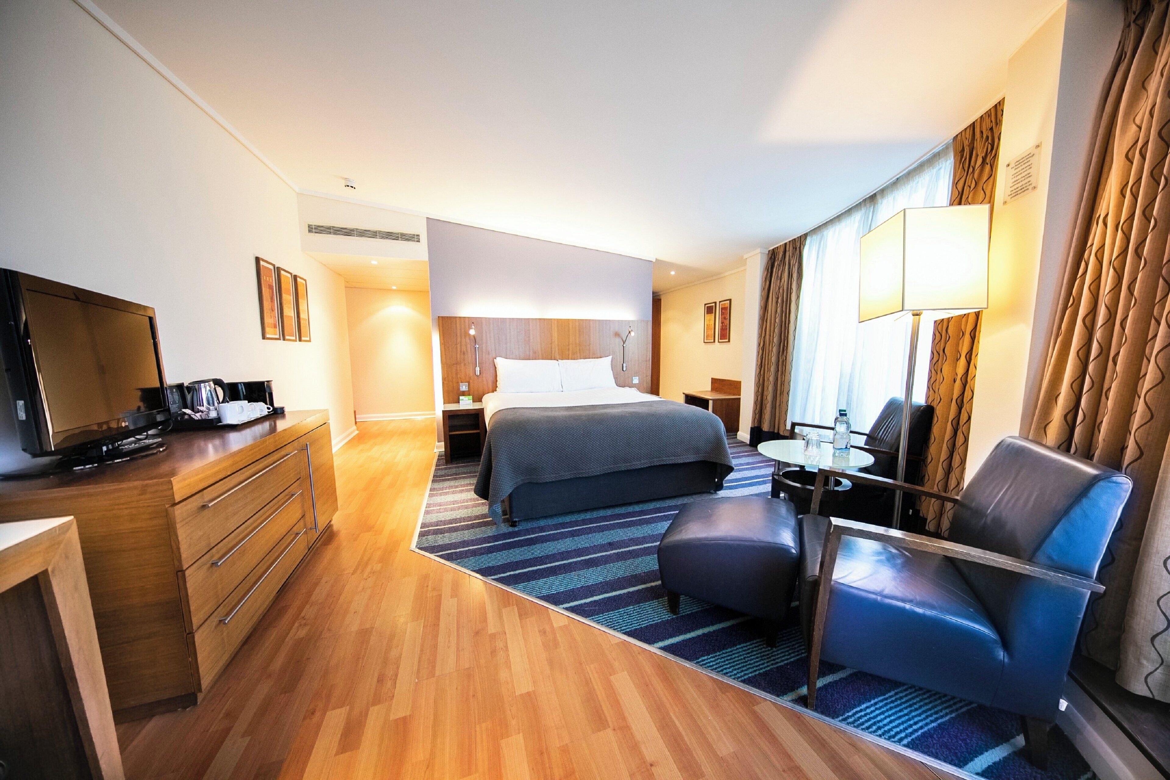 Quarto de hotel com cama, escrivaninha, cadeira, televisão e janela com cortinas.