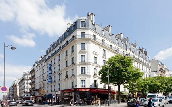 Um edifício de esquina com fachada branca, várias varandas e uma placa visível 'AVIA HOTEL'.