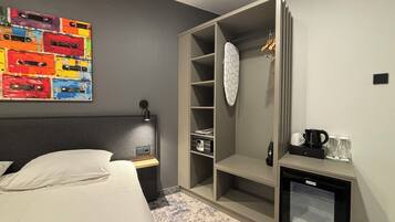 Quarto de hotel com cama, guarda-roupa, mini-frigorífico e máquina de café.
