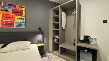 Quarto de hotel com cama, guarda-roupa, mini-frigorífico e máquina de café.