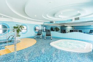 Uma piscina interior com piso em azulejo, uma banheira de hidromassagem e áreas de estar.