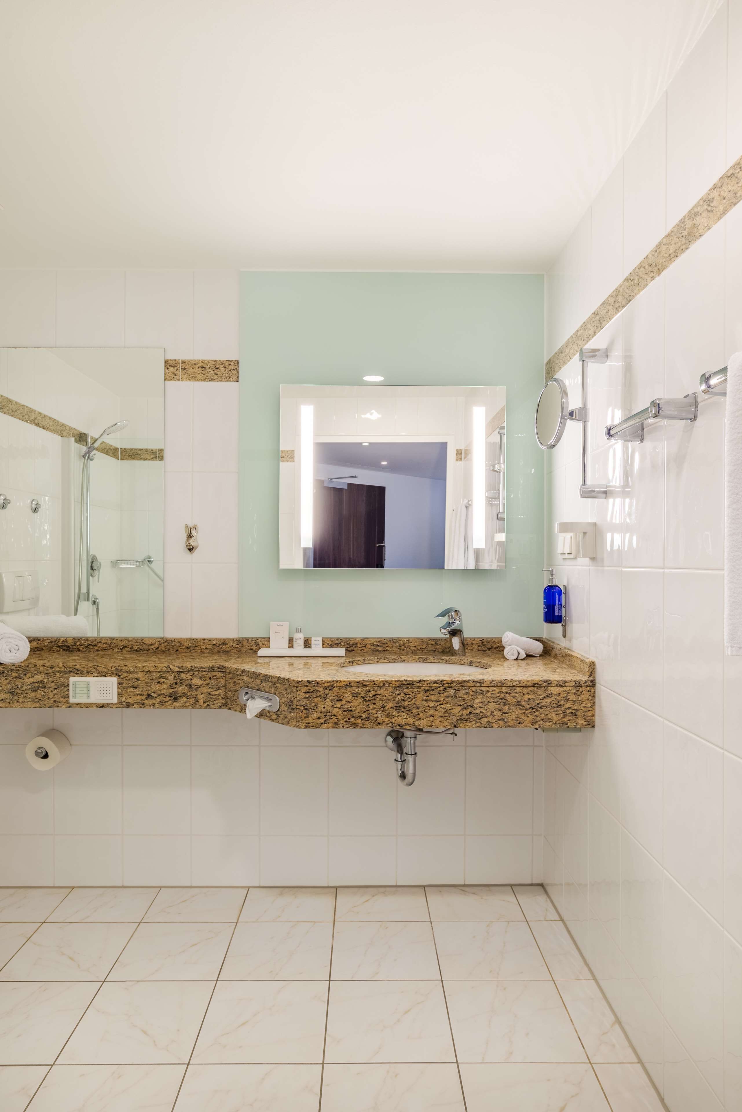Uma casa de banho moderna com bancada de granito, um espelho grande e zona de duche.
